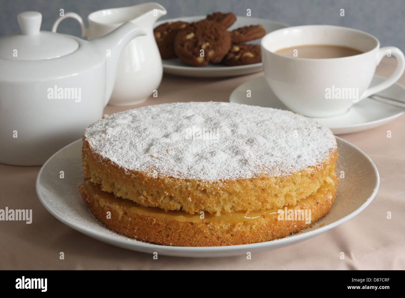 Afternoon tea. A freshly baked sponge cake dominates the photo, a ...