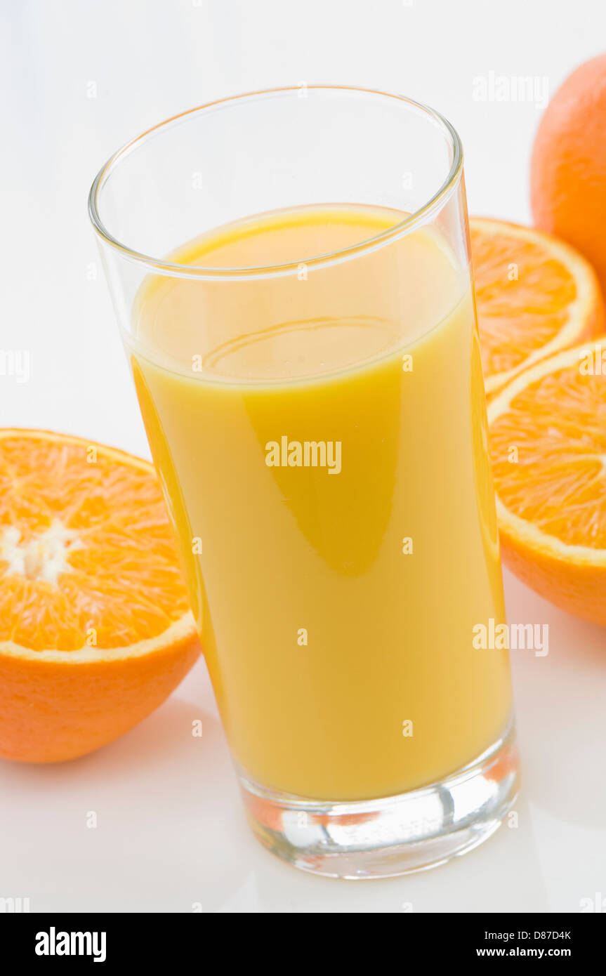 Glass of orange juice besides oranges on white background, close up ...