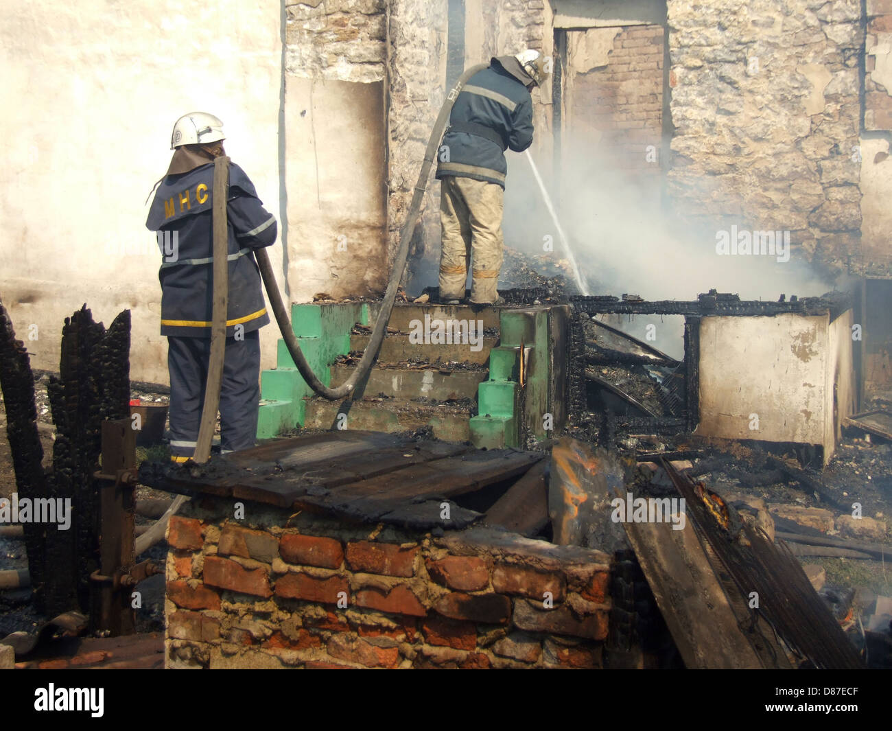Smoldering remains of a ghetto house with a fireman spraying water ...