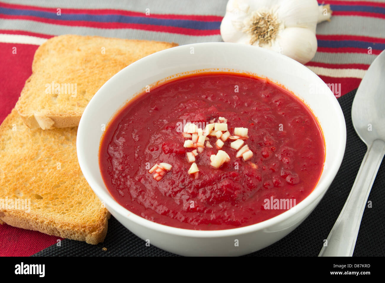 Red mashed beet soup with chopped garlic in white bowl. Entire garlic ...