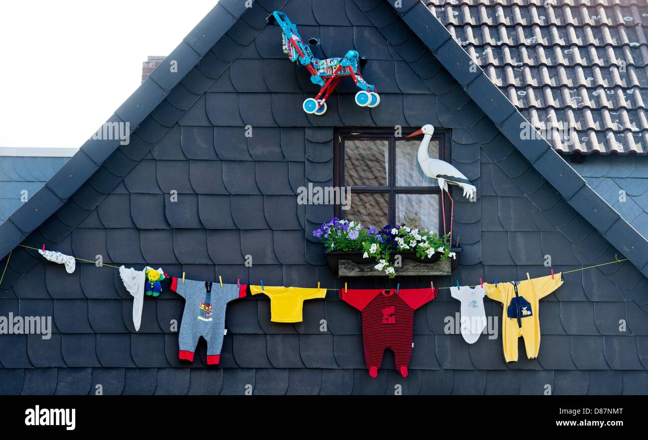 Baby clothes, a stroler and a wooden stork hang on the wall of a house ...