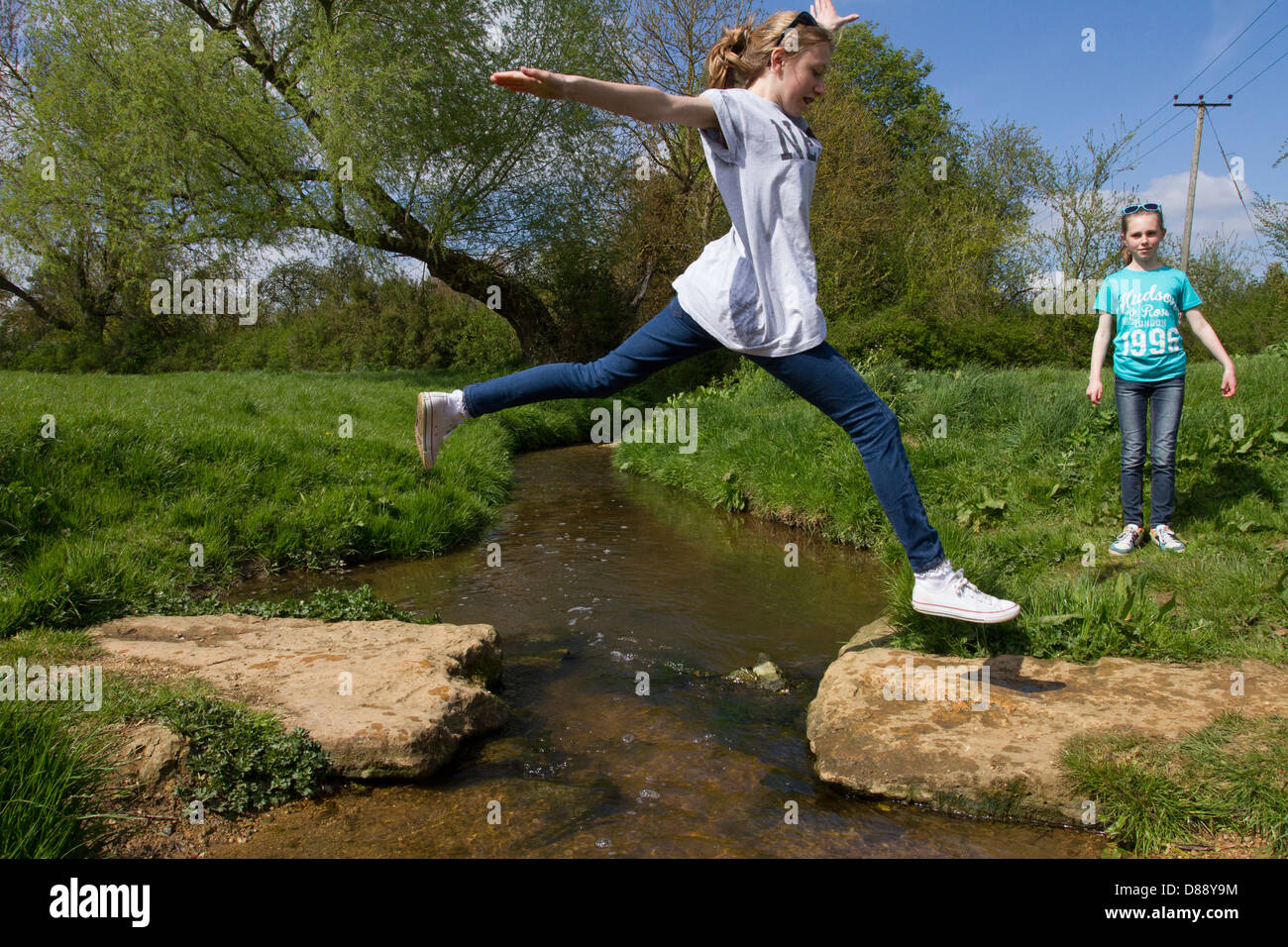 young girl jumping over a stream, another girl watching Stock Photo - Alamy