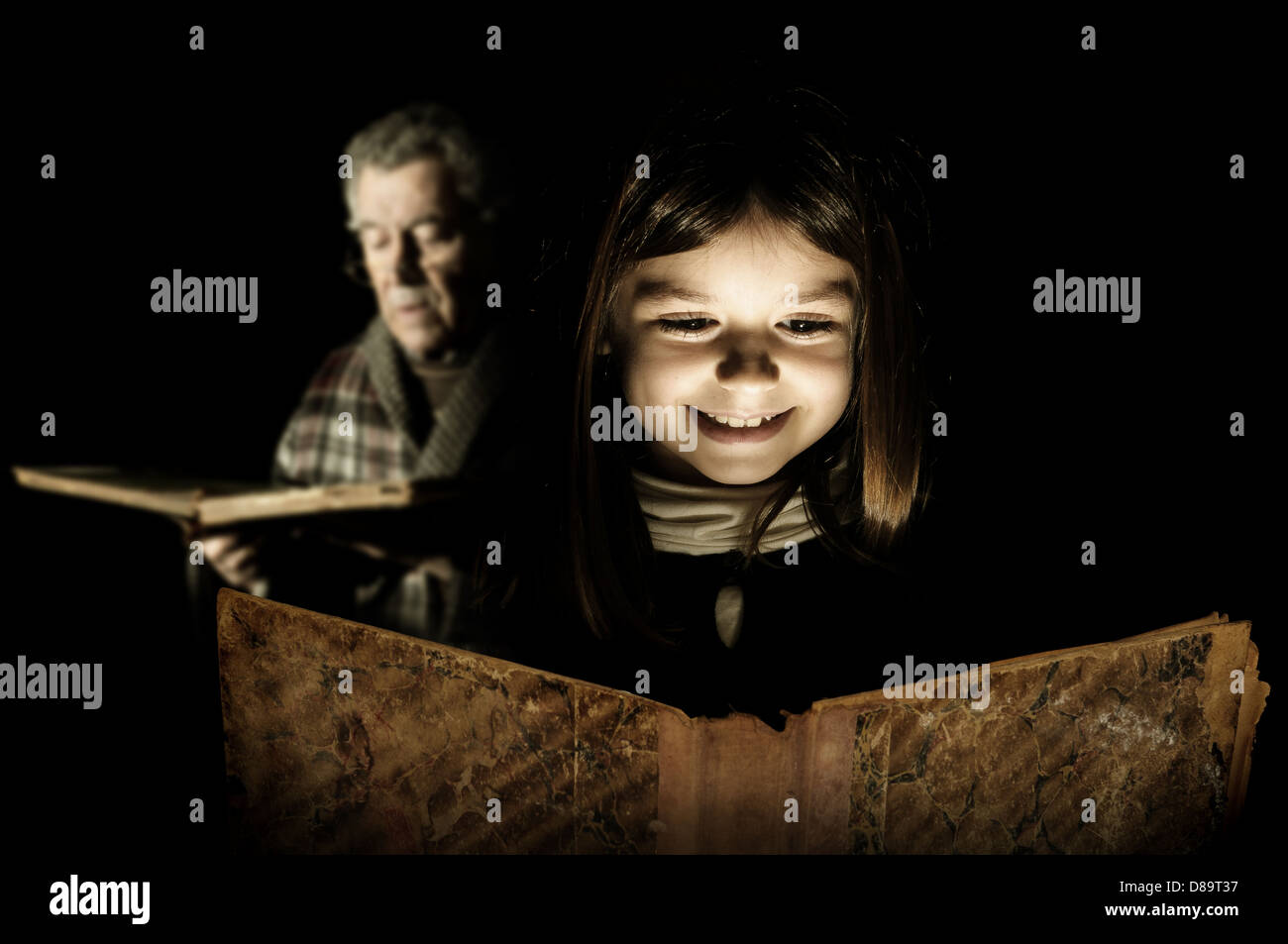 Young girl reading a very old book with grandfather in the background ...