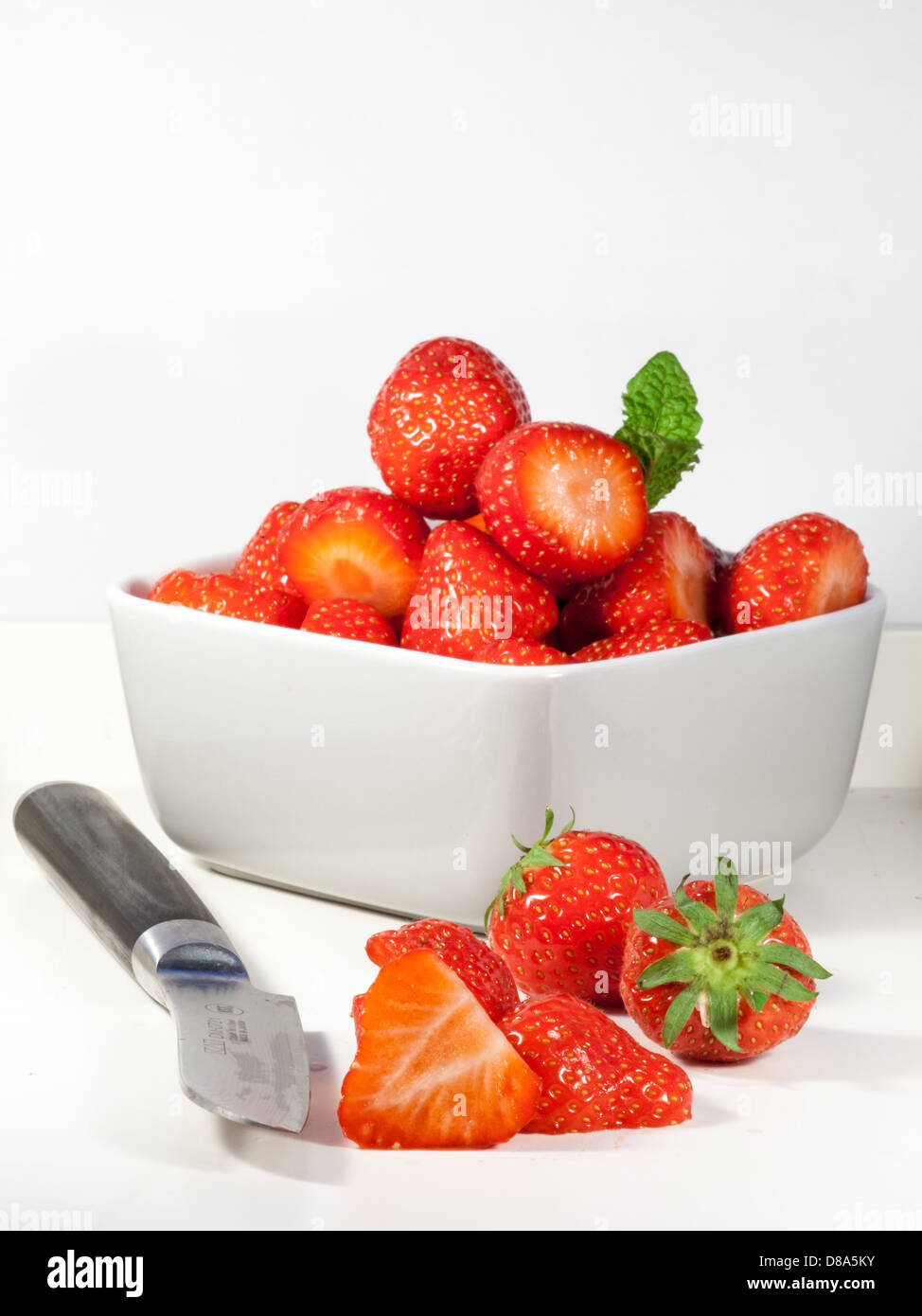 freshly sliced strawberry and fruit knife on a white cutting board with ...