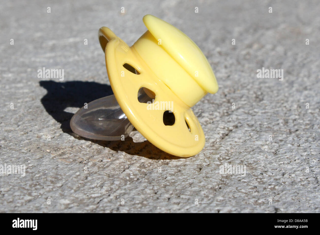A baby pacifier rests on a sidewalk, lying on its side with a clear ...