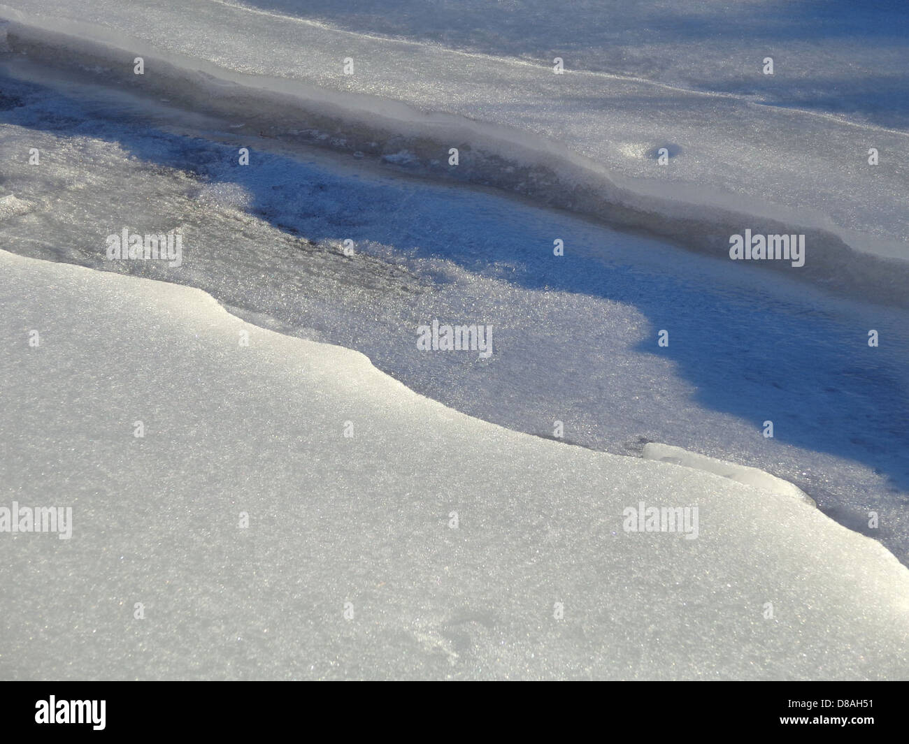 A winter scene depicting a frozen stream, covered in snow and ice. The ...