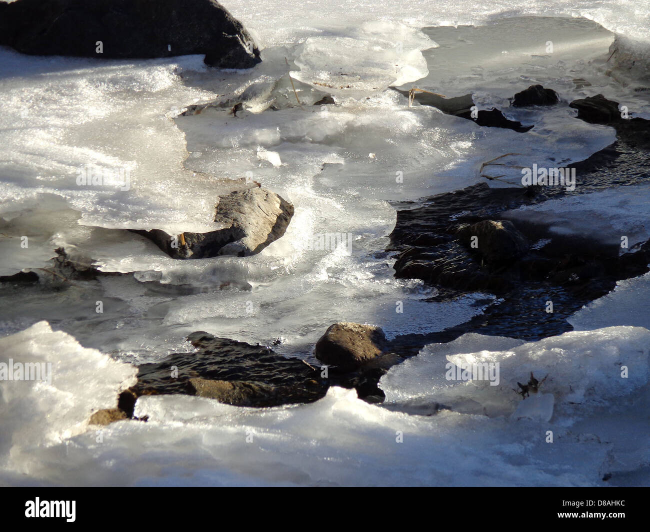 A photograph capturing water flowing beneath melting ice in a stream ...