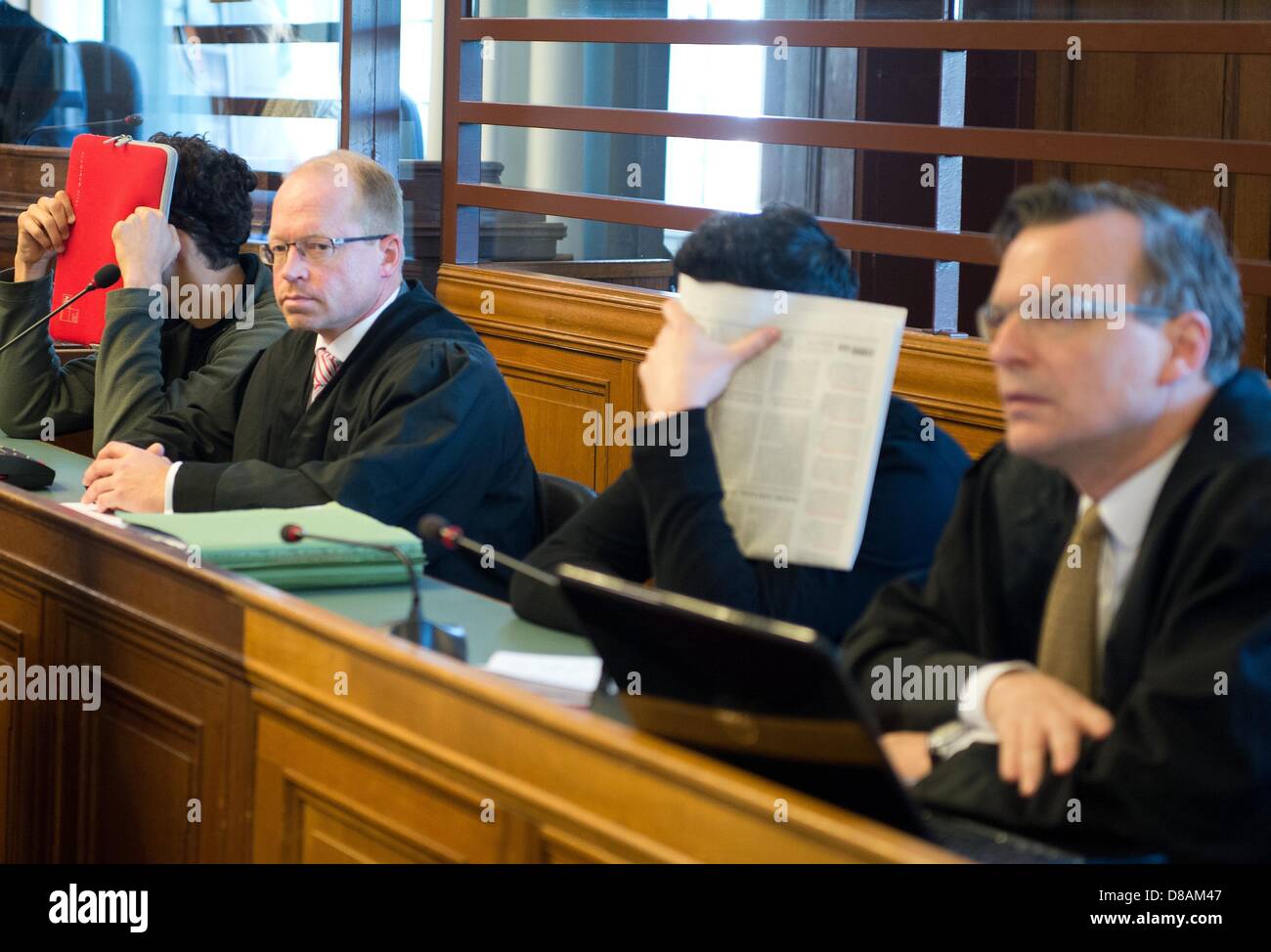 Two defendants hide their faces behind newspapers before the beginning ...