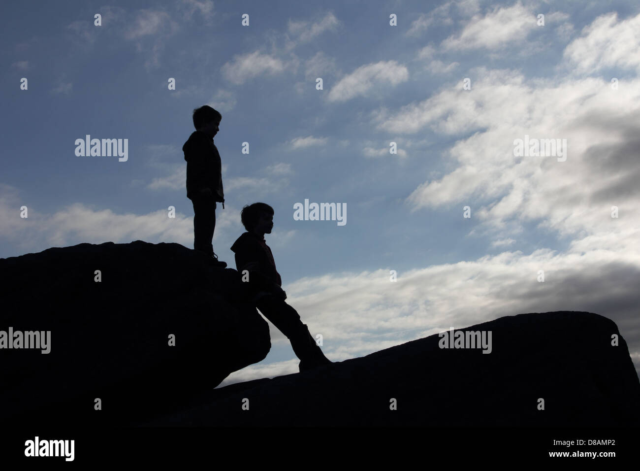 two young boys in silhouette standing on two boulders looking into the ...