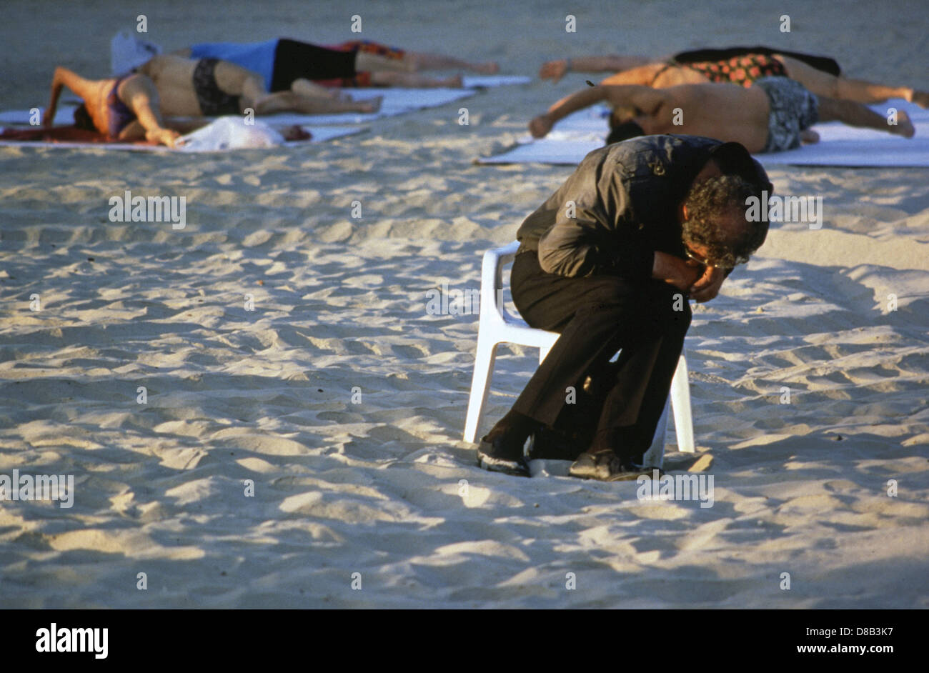 A homeless person sleeping on a chair with elderly people stretching at ...