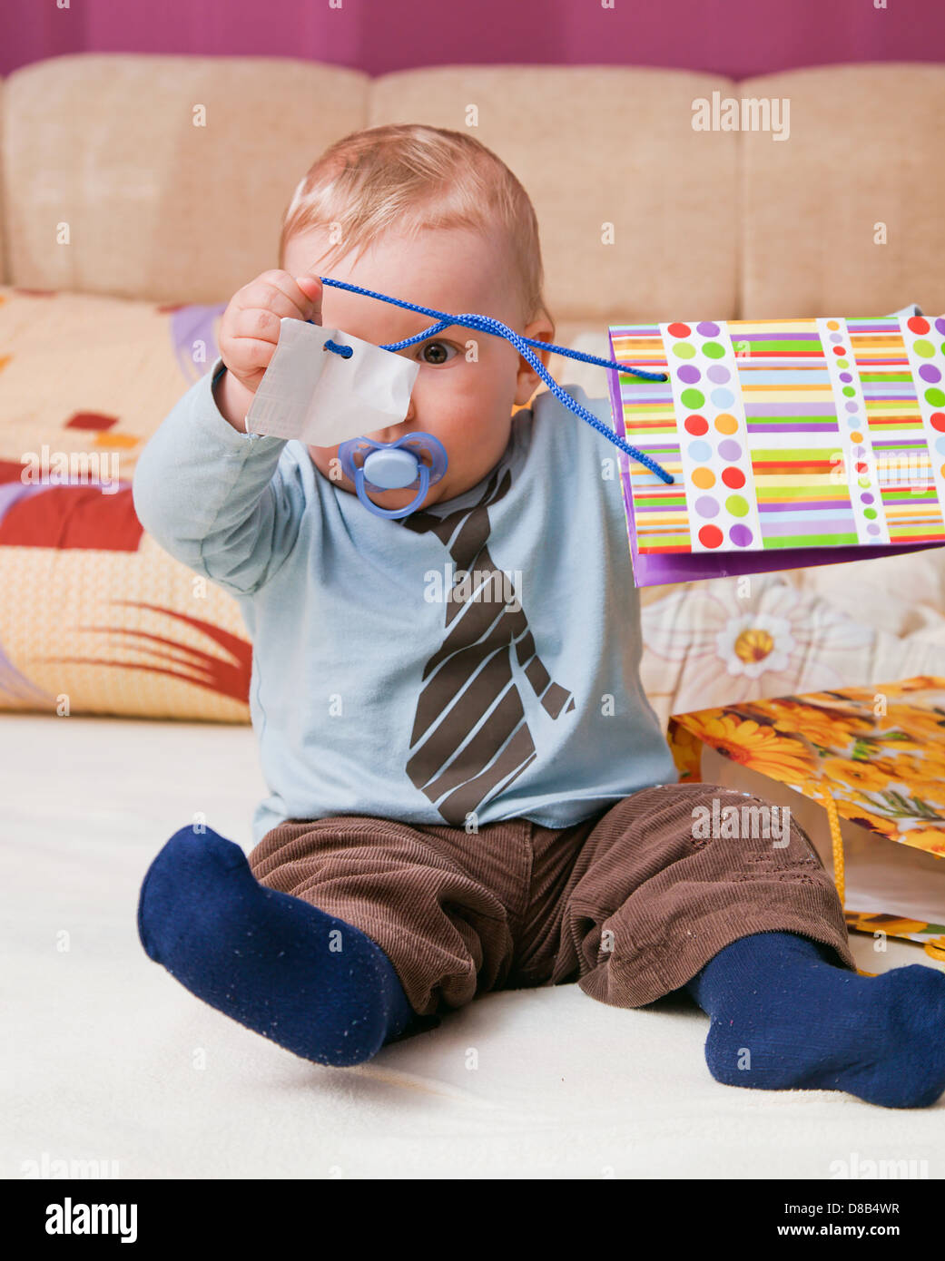 Young baby boy with a dummy in his mouth playing with colorful gift ...