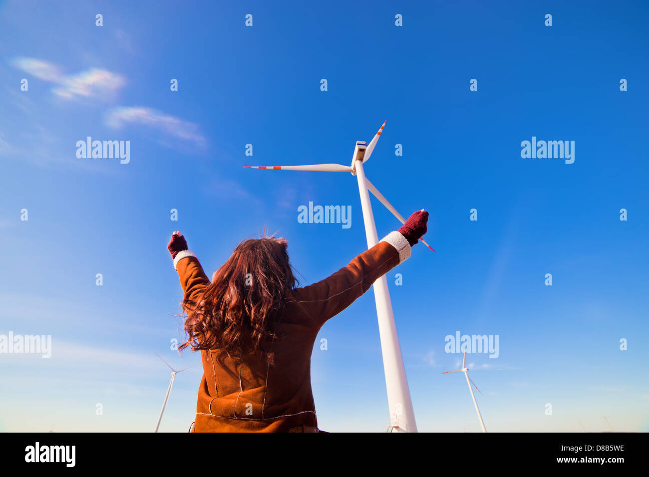 Young happy woman with hands up looking at wind turbines, eco energy ...