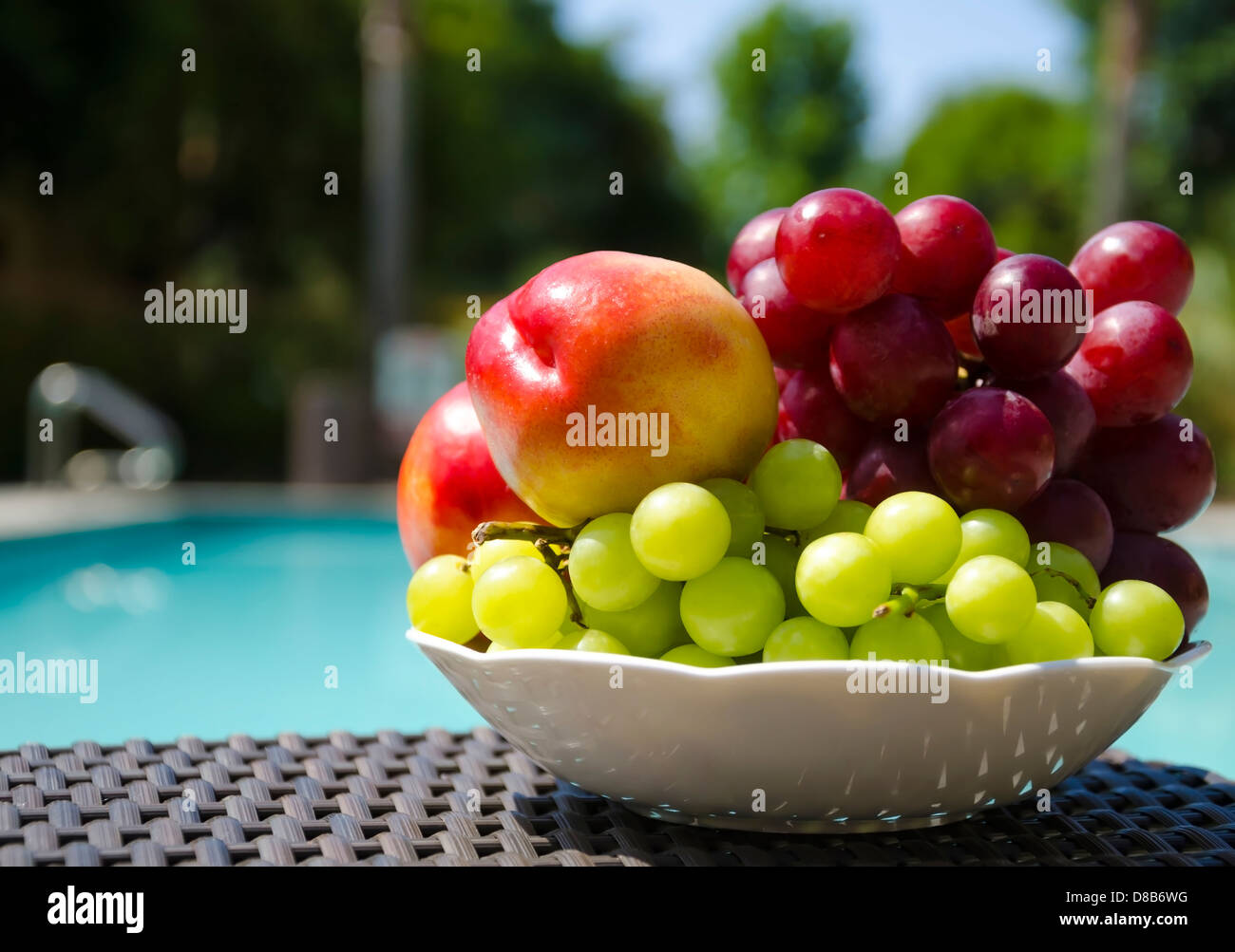 Two peaches and grape in white plate on table by the swimming pool ...