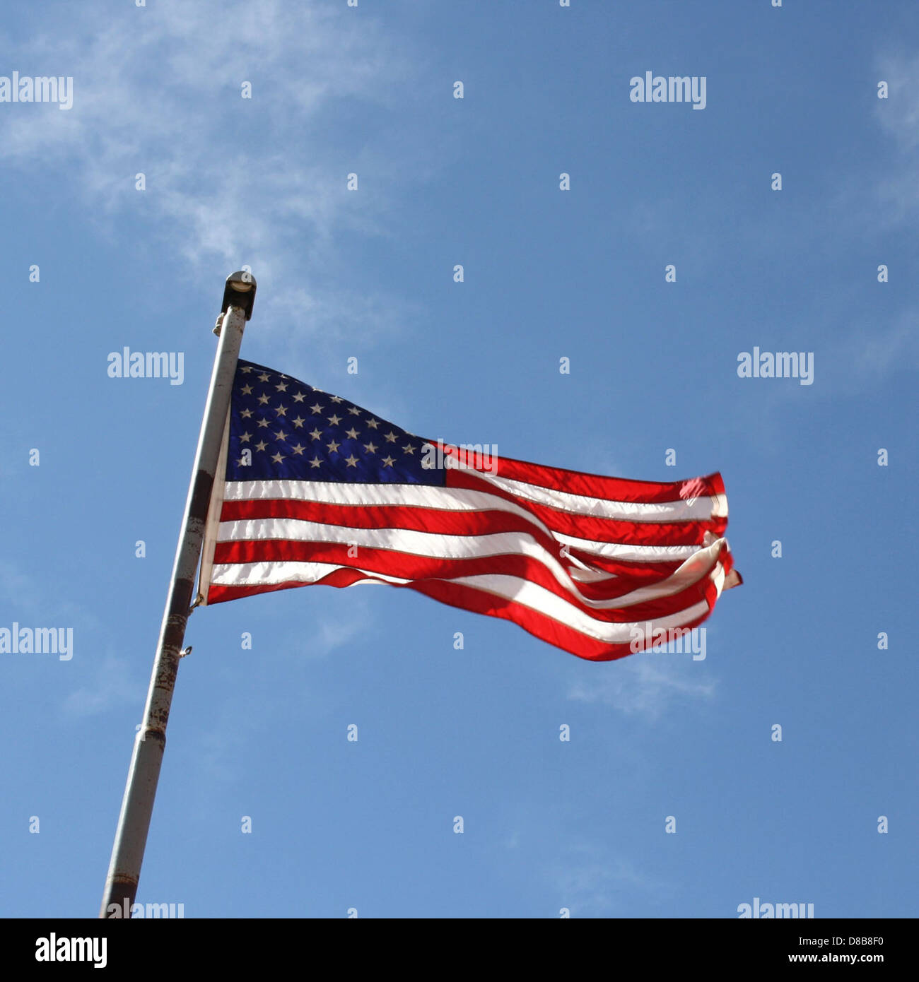 An American flag waves proudly atop a flagpole against a clear blue sky ...