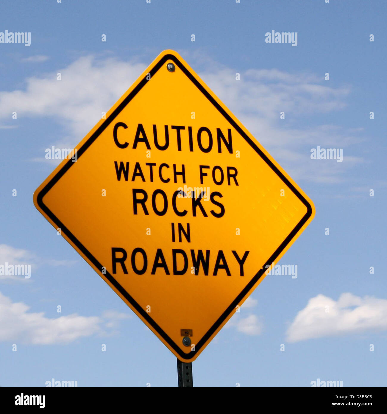 A caution sign warning of rocks in the roadway. This safety sign alerts ...