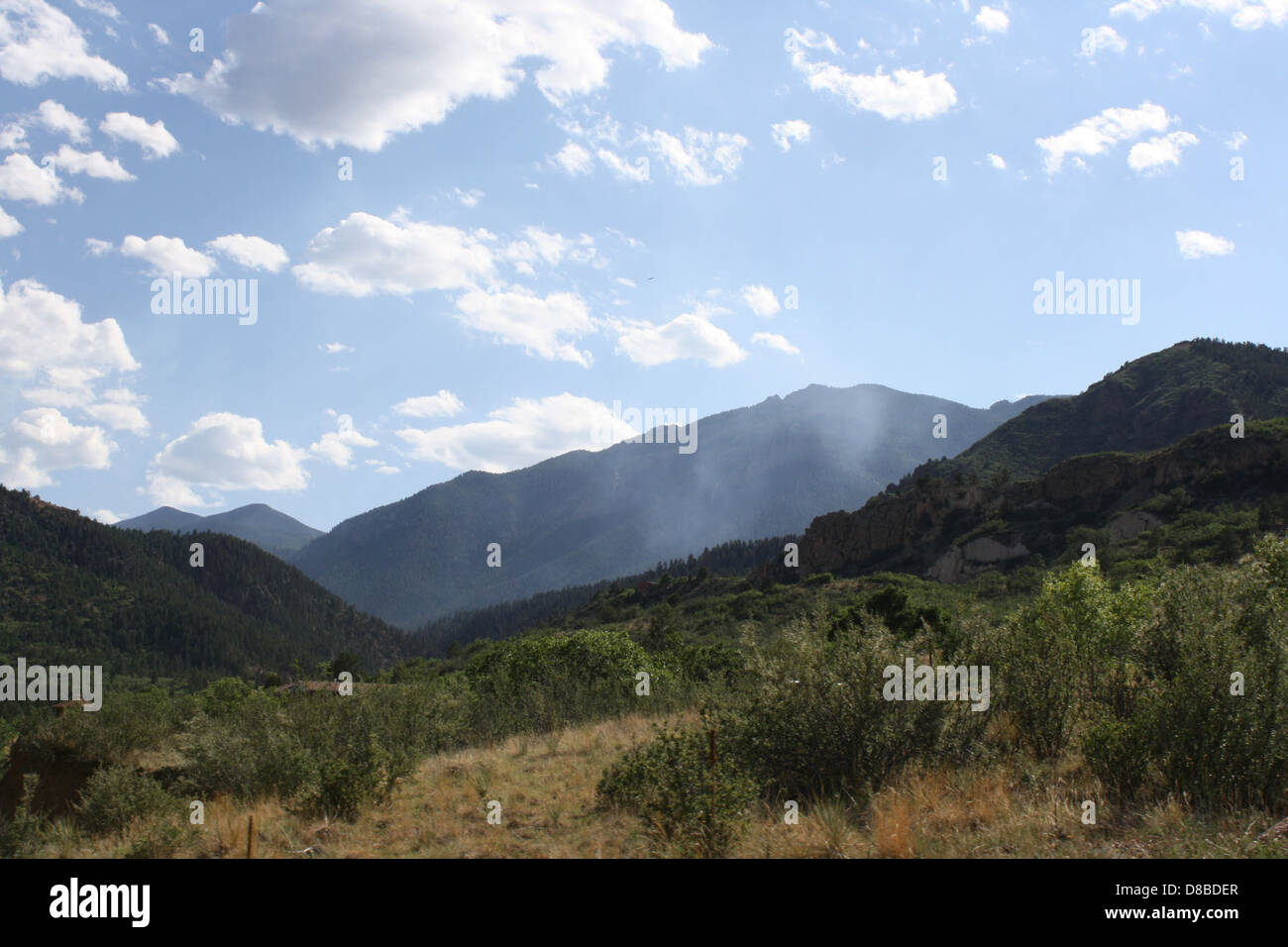 A wildfire burning in a valley, with thick smoke rising from the flames ...