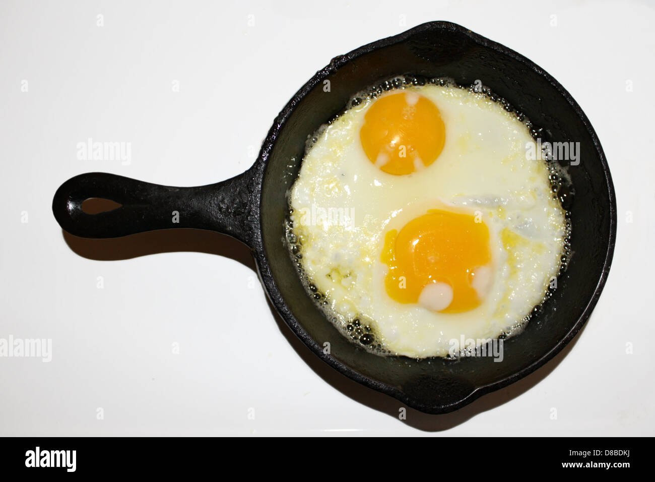 A classic breakfast dish of fried eggs cooked sunny side up in a cast ...