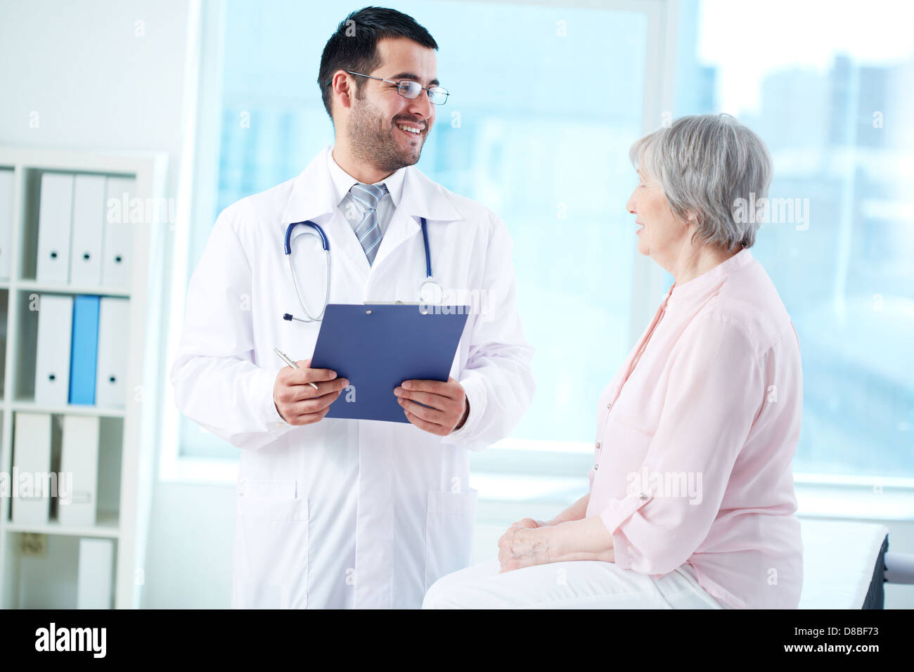 Confident doctor with stethoscope and clipboard interacting with his ...