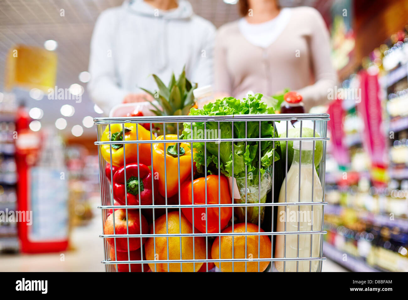Image of cart full of products in supermarket being pushed by couple ...