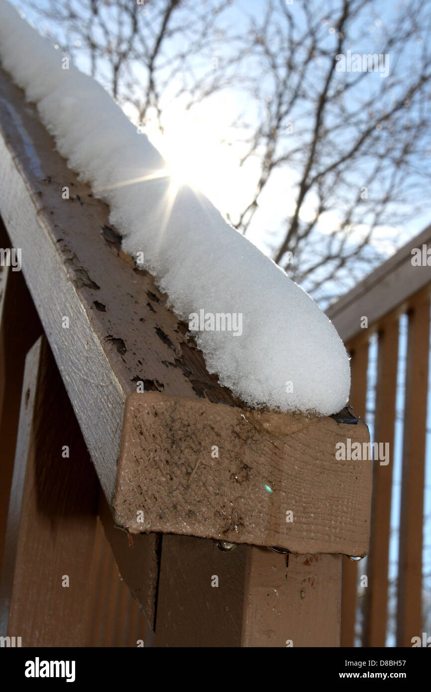 Snow melting on the railing of a deck, showcasing the transition ...