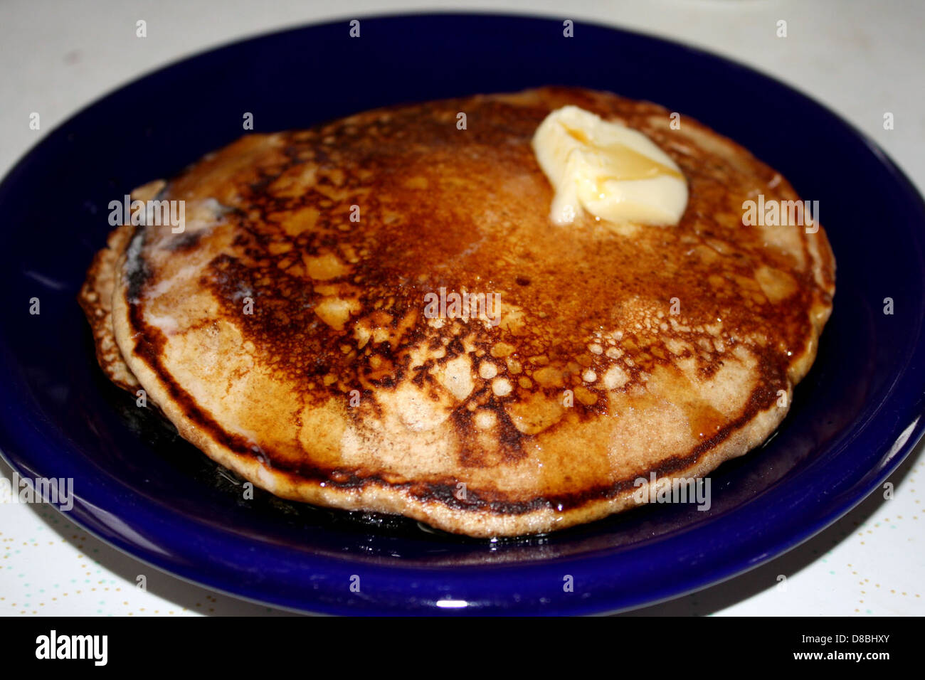 A stack of fluffy pancakes topped with melted butter and drizzled with ...