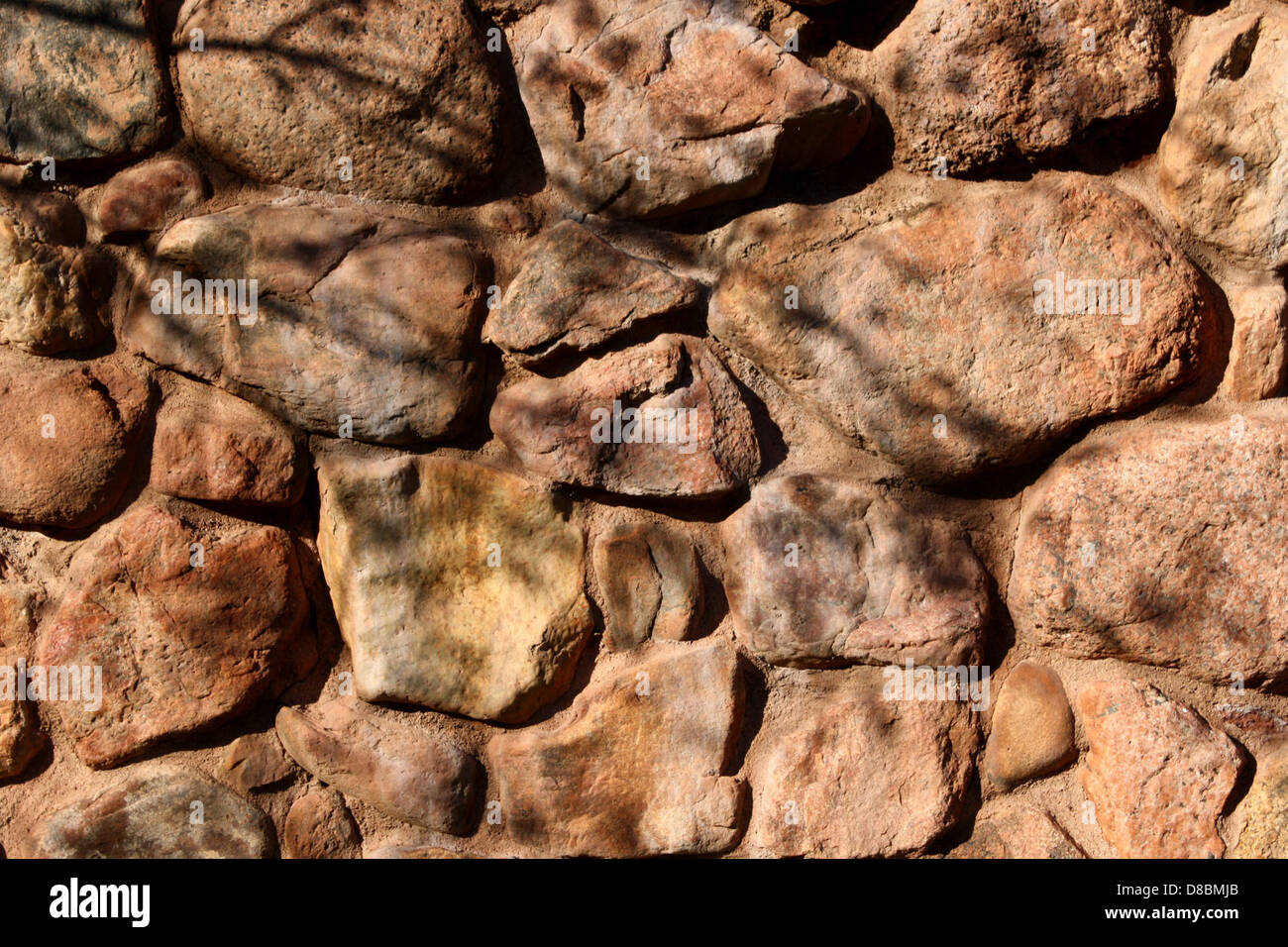A textured image of a rock wall with tree branch shadows casting over ...