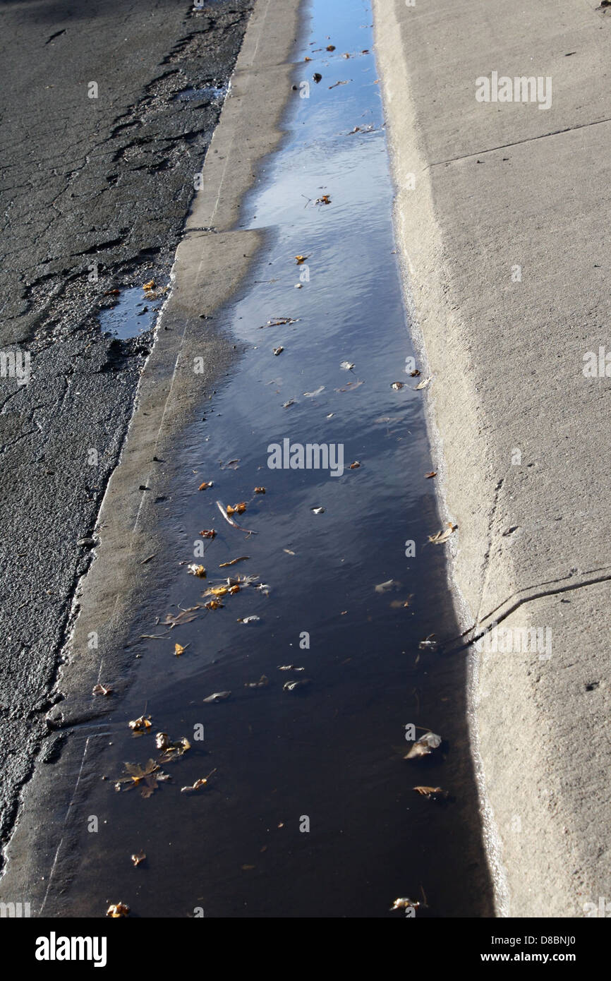 A sidewalk gutter filled with rainwater, showing urban drainage in ...