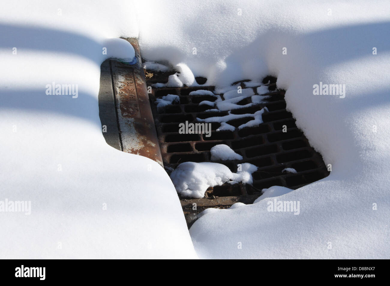 A storm drain covered in snow, with the surrounding area also blanketed ...