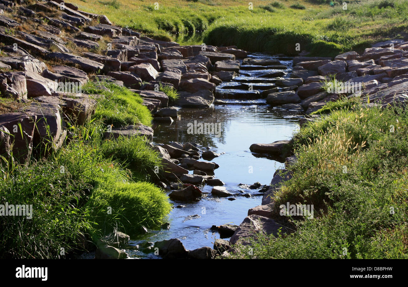 A serene stream flows through a natural landscape, with a waterfall ...