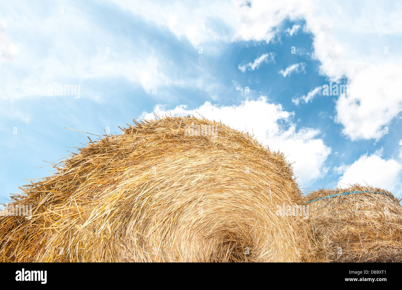Haystack in foreground, blue sky with clouds in background. Roll of dry ...