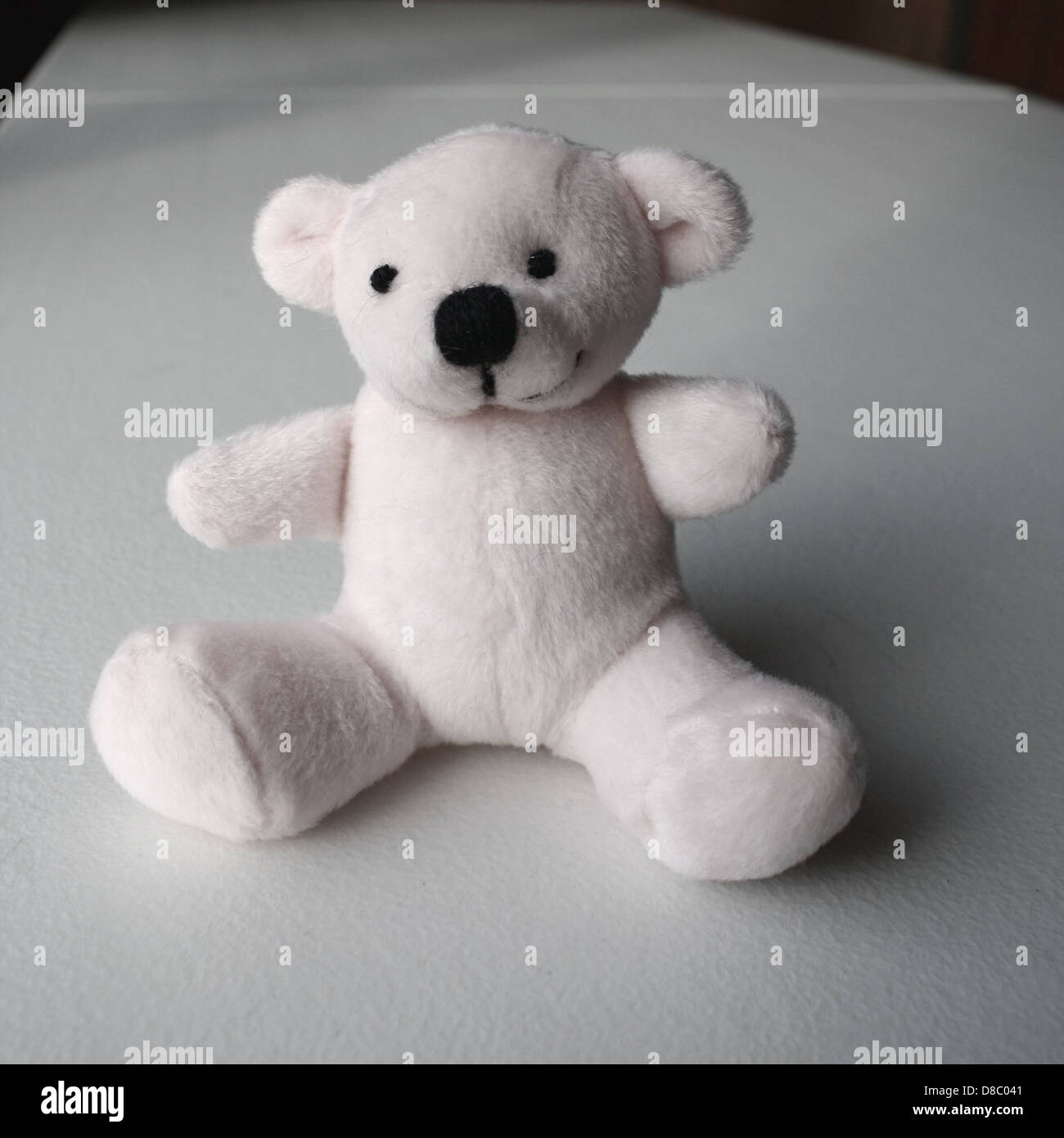 A soft white teddy bear placed on a neutral-colored surface. The plush ...