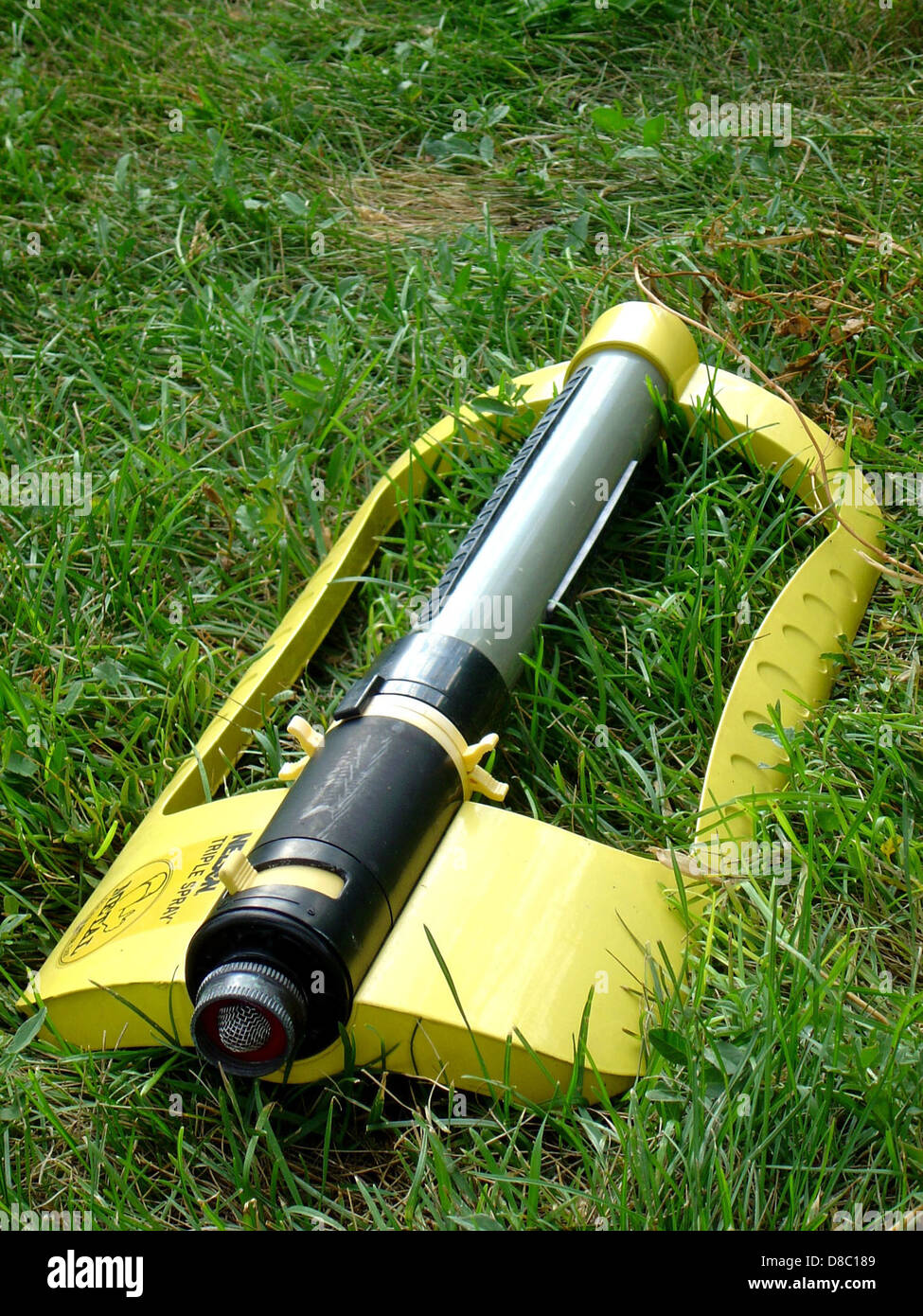 A yellow sprinkler positioned on a grassy field, spraying water across ...