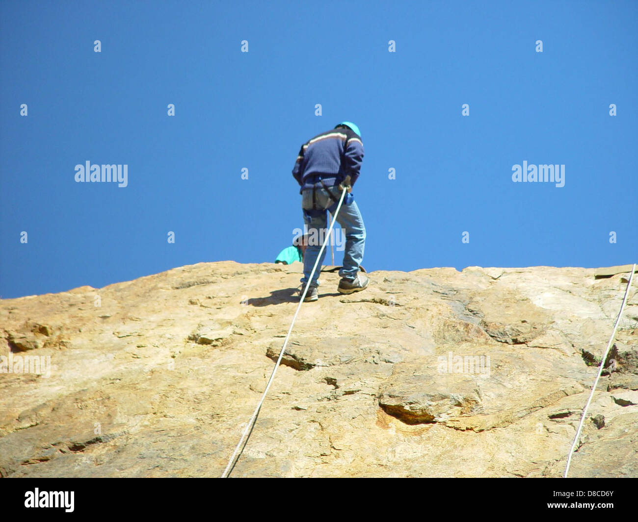 This image depicts a mountain climber abseiling down a steep cliff ...