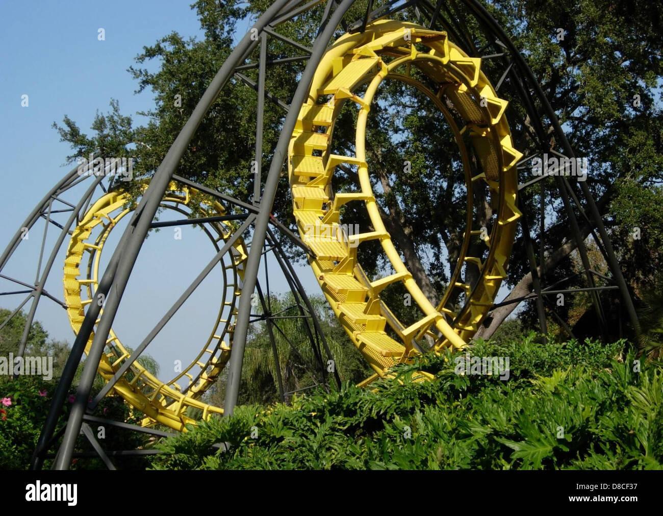 A vibrant yellow roller coaster track twisting through a wooded area ...