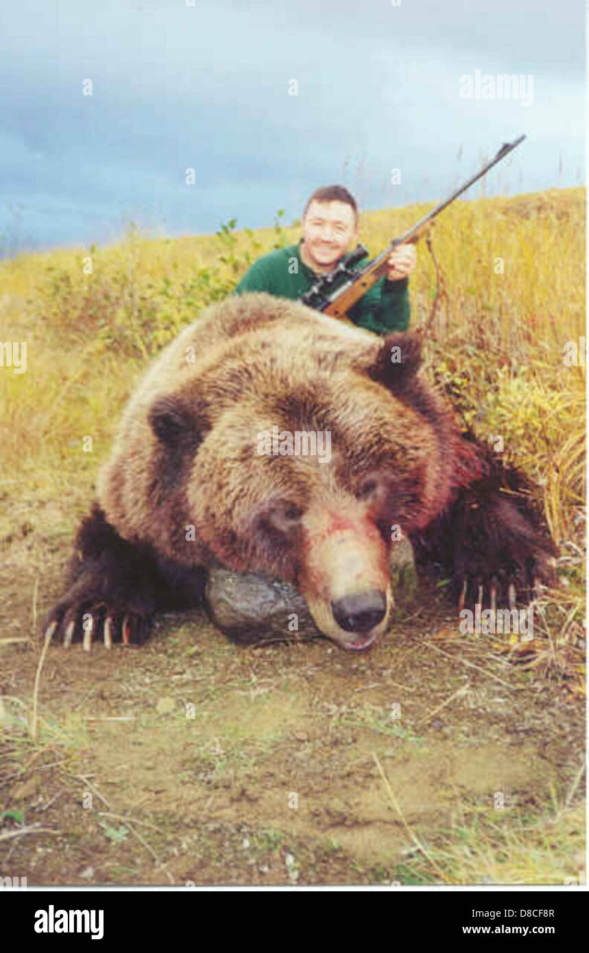 A bear hunter stands beside a bear, captured in a natural outdoor ...
