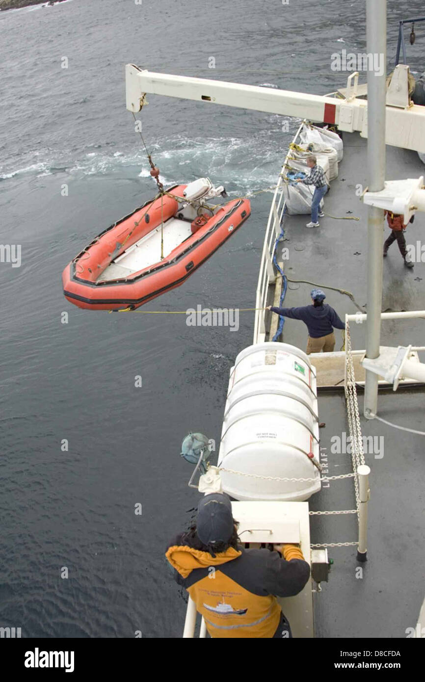 A large ship is offloading a skiff boat onto the shore. The skiff, a ...