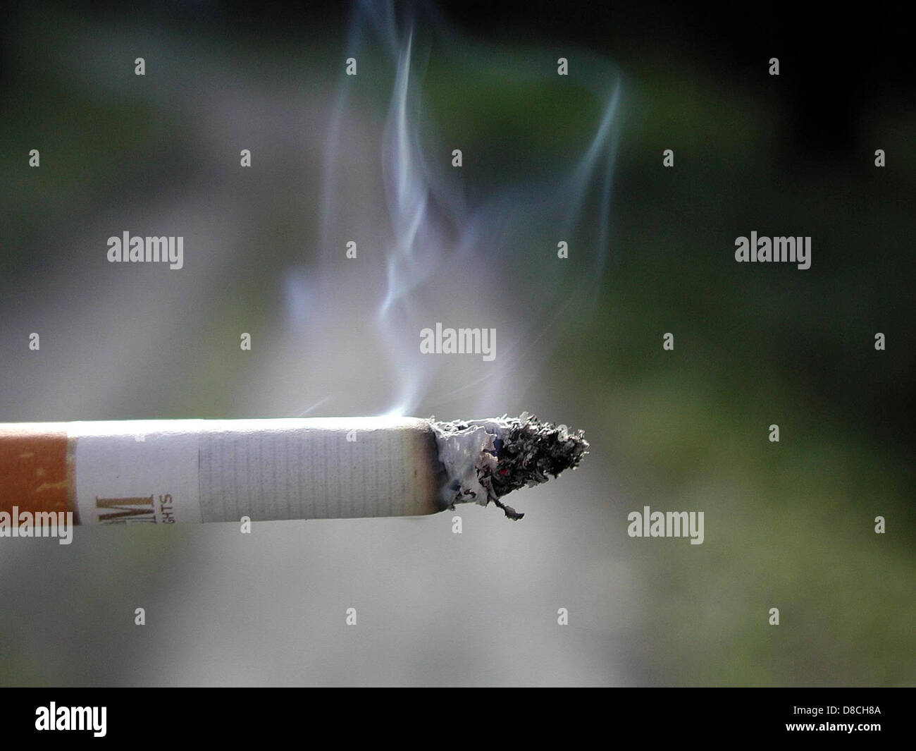 A person smoking a cigarette, with smoke rising from the tip. The image ...