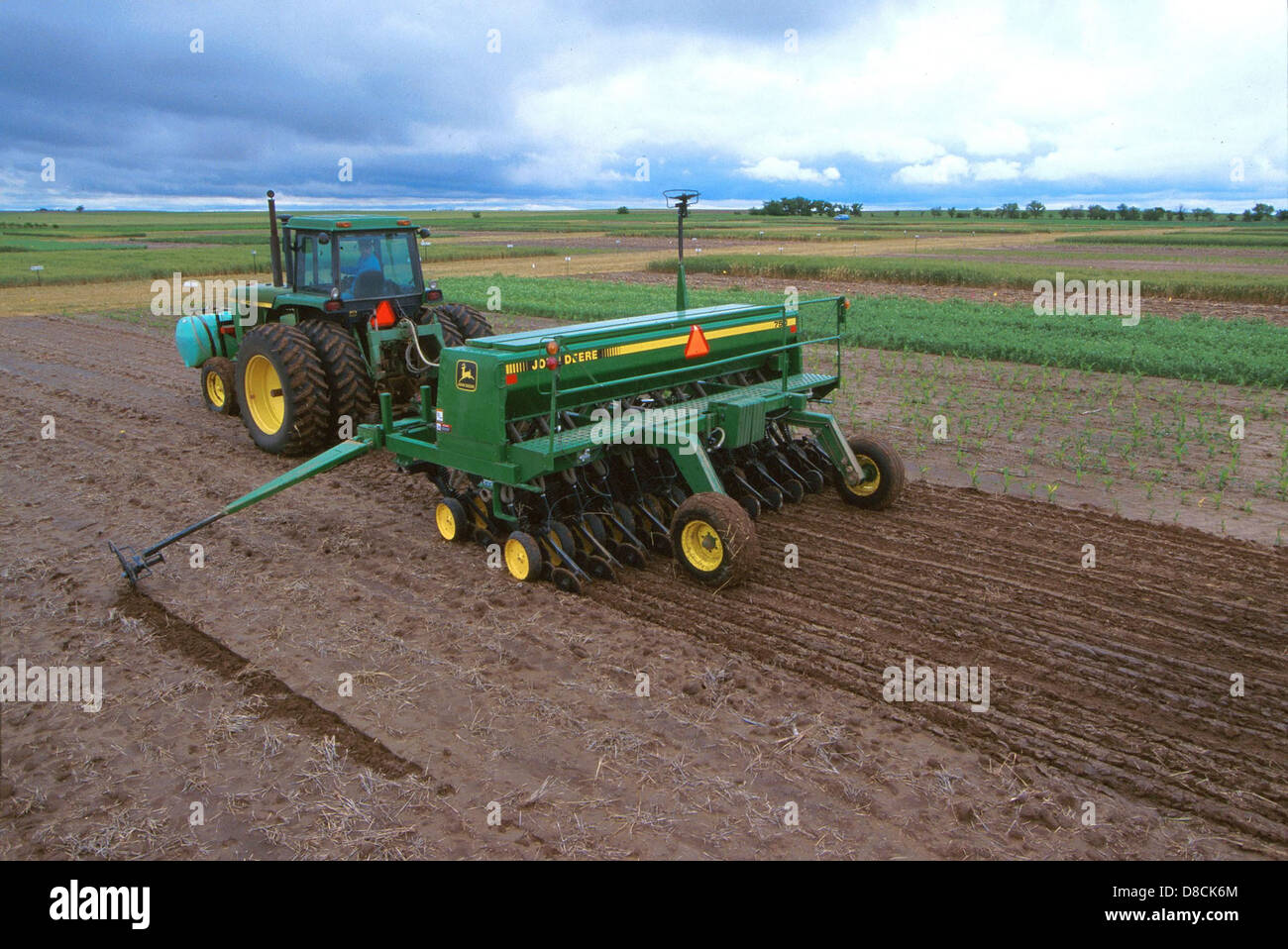 A farmer using a tractor to plant crops on a field. The image captures ...