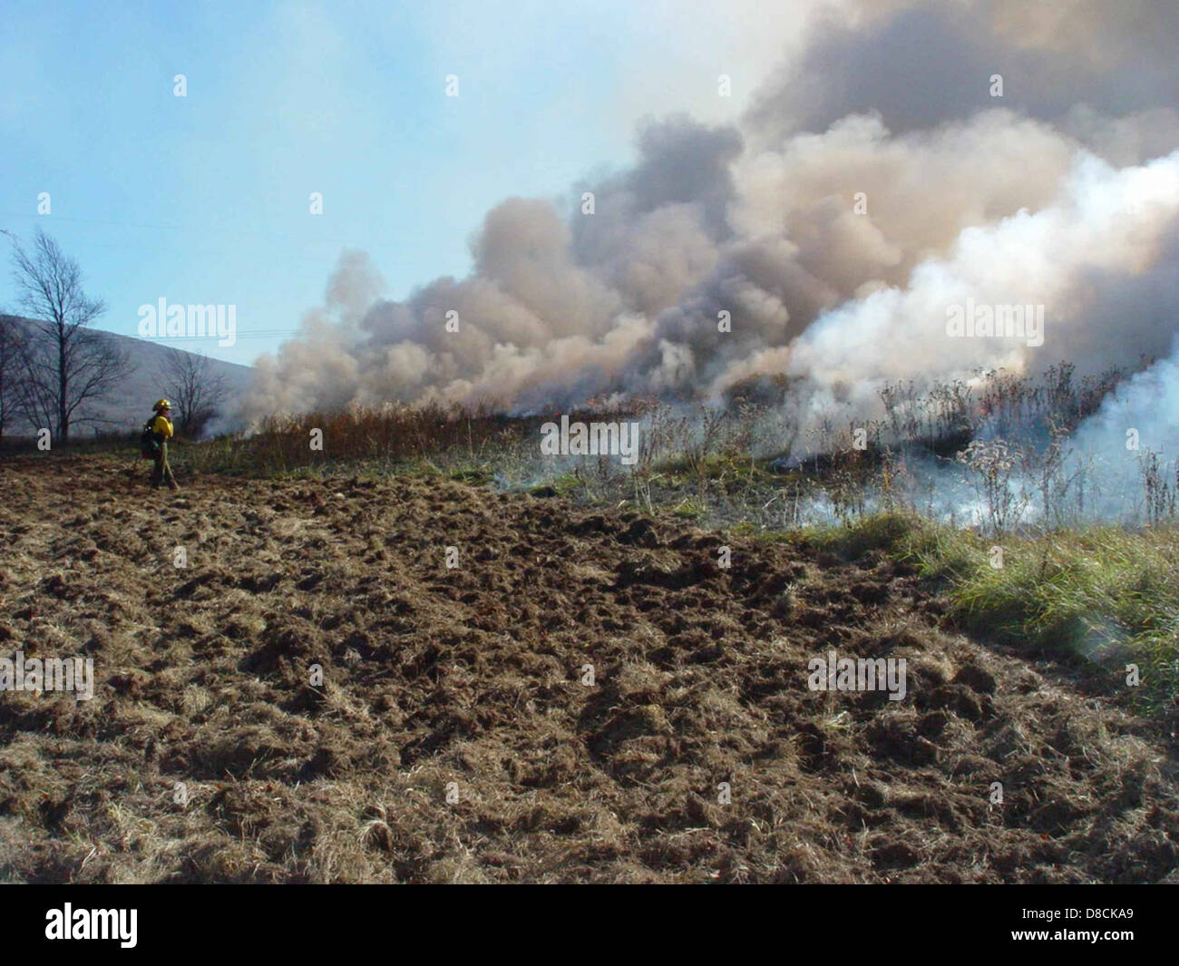 A firefighter approaches a wildfire on a hill during the summer, where ...