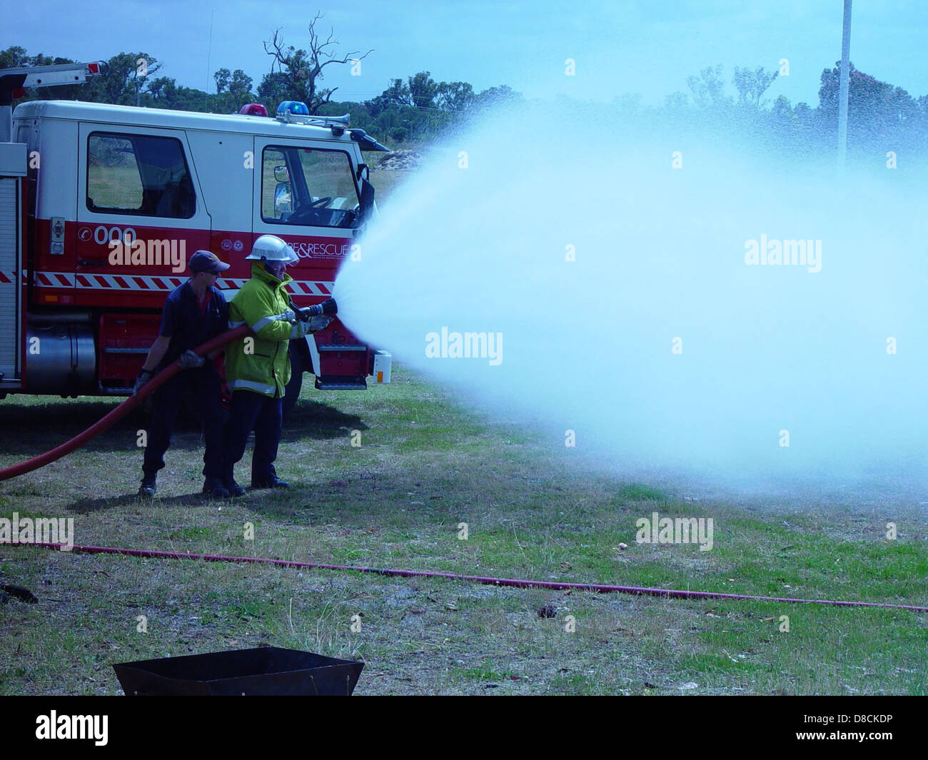 A fire hose spraying water at maximum force to combat a fire. This ...