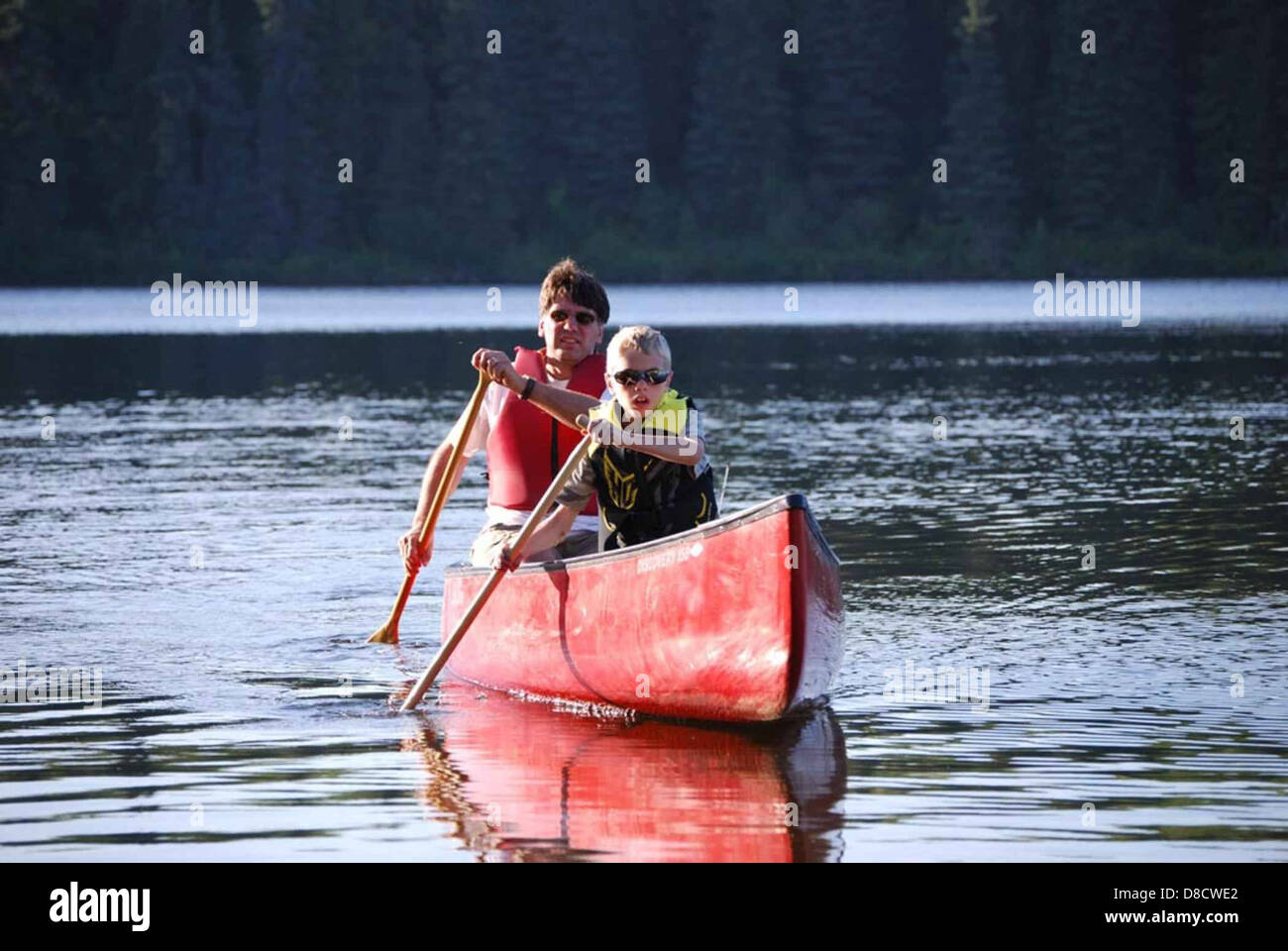 A man and a child are paddling a sport canoe across calm water. The ...