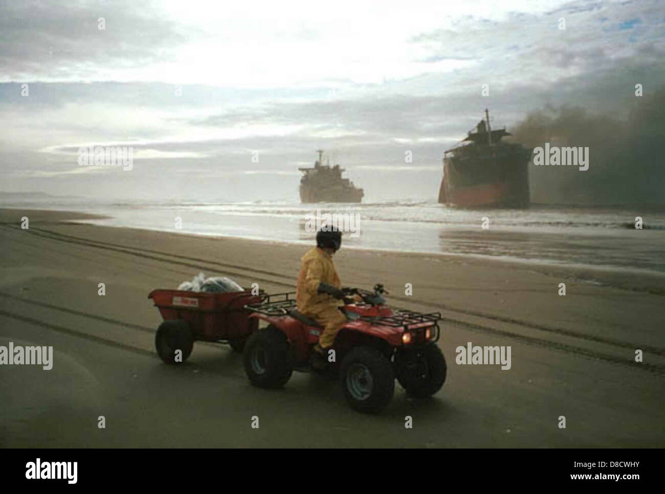A man drives a small engine vehicle on the beach, observing a ship in ...
