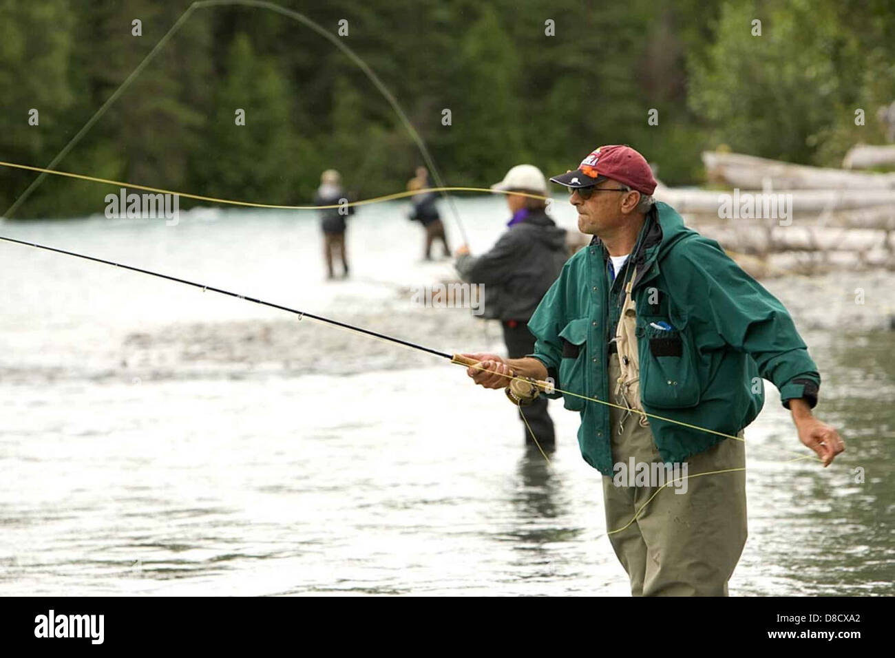 A man fly fishing in a river, using a fly rod to cast a line into the ...