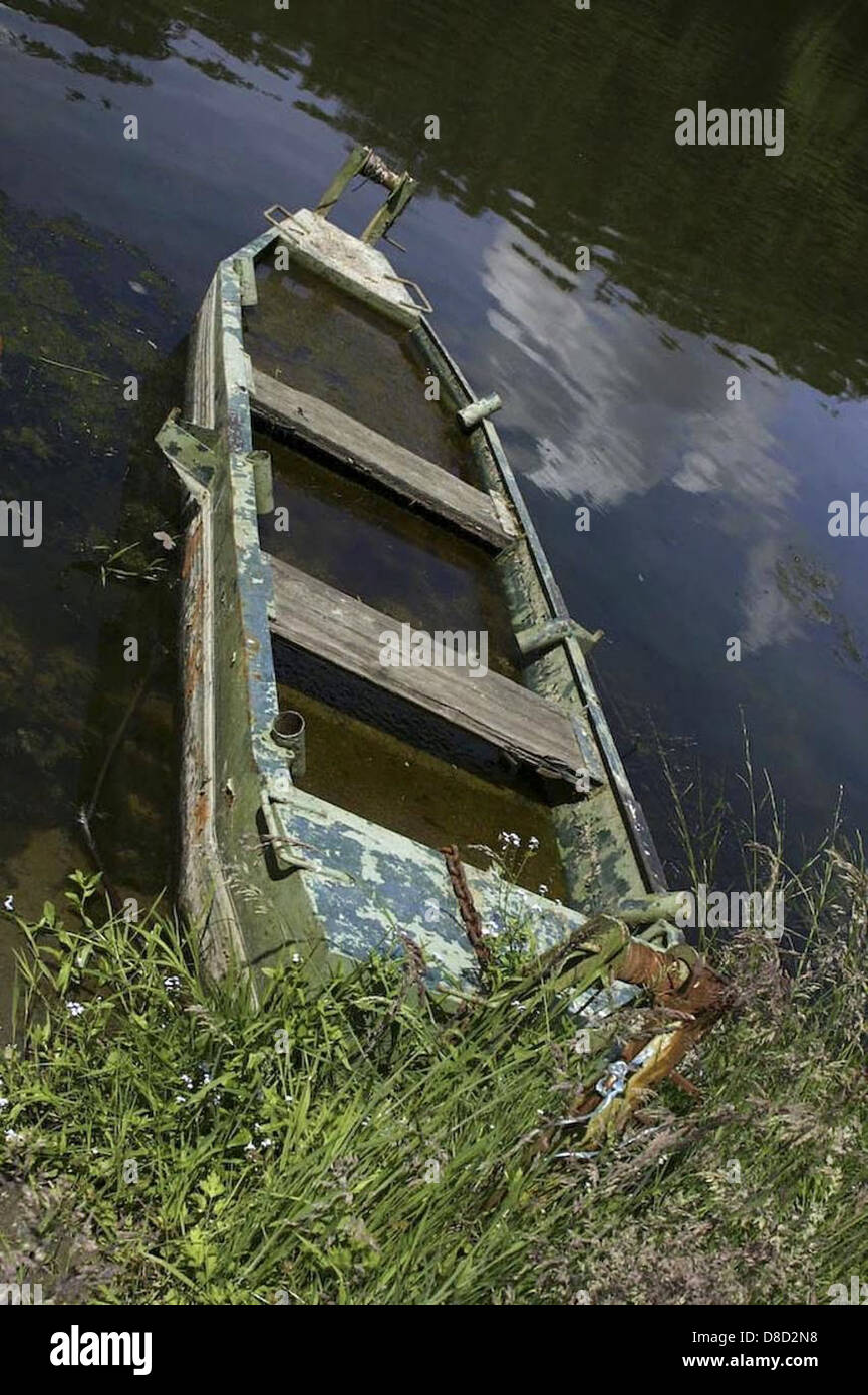An old, weathered wooden boat is seen floating on a river, reflecting ...