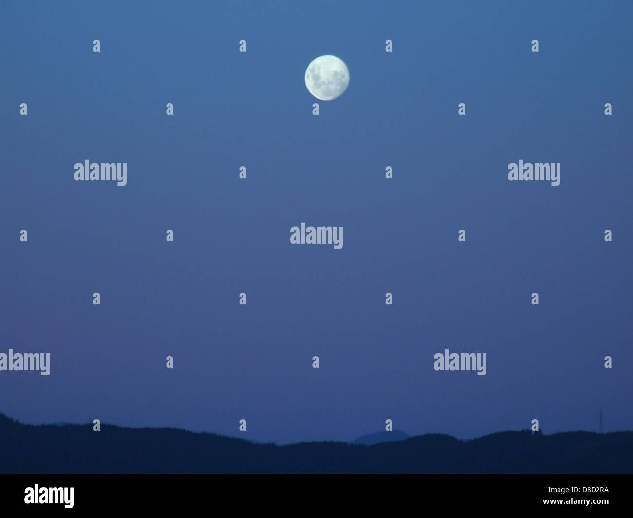 This image features a full moon set against a blue background. The moon ...