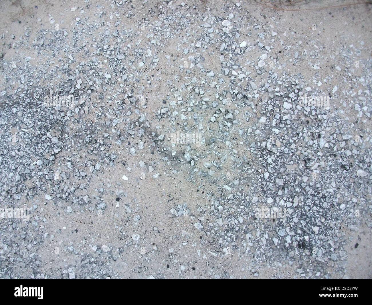 A pavement surface covered in sand, likely due to wind or environmental ...