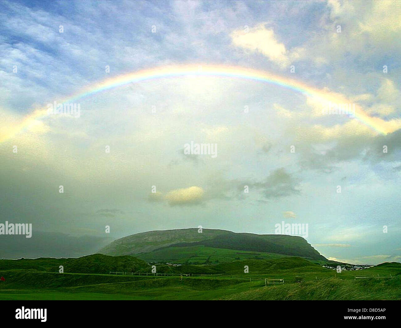 The landscape depicts a vibrant rainbow arching across the sky over a ...