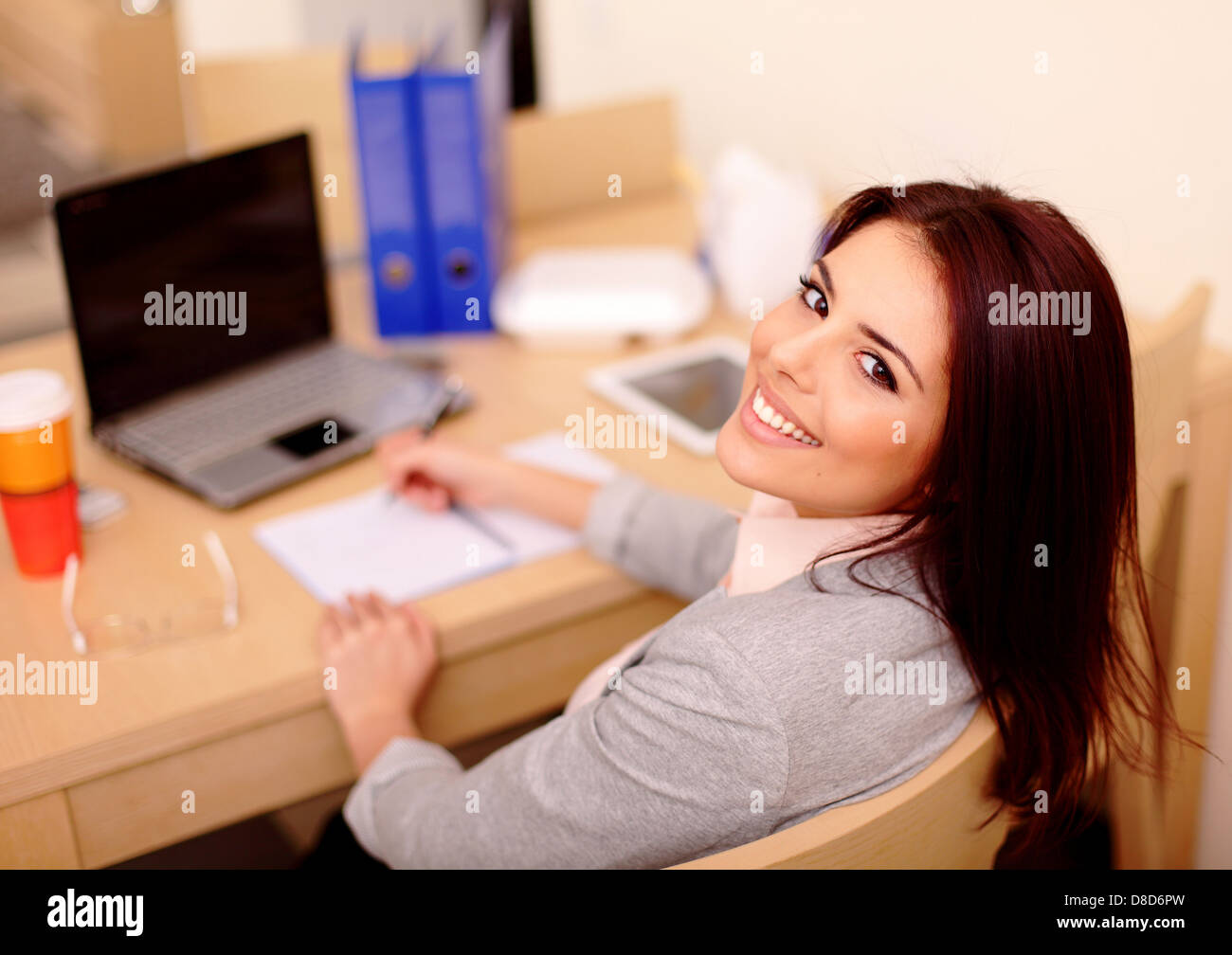 Young businesswoman sitting at desk and working. Smiling and looking ...