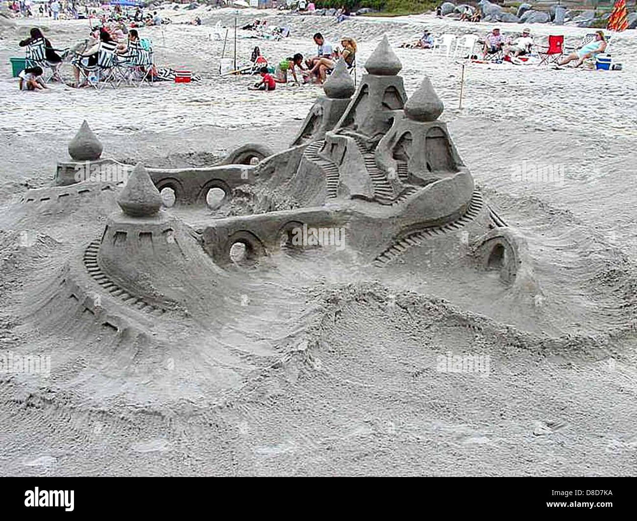 A sandcastle stands on the beach, shaped from sand along the shoreline ...