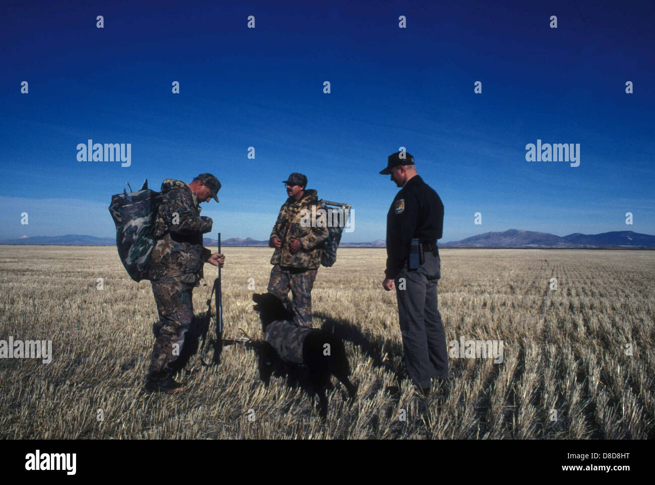 Service law enforcement officer speaks with two duck hunters with a dog ...